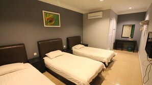 Quarto de hotel com três camas, uma pequena escrivaninha, um espelho e um aparelho de ar condicionado.