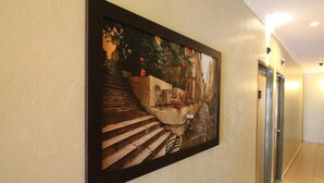 Um corredor com um quadro emoldurado retratando uma cena de rua, uma porta e um luminário.