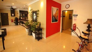 Um saguão de hotel com parede de destaque vermelha, um relógio, um extintor de incêndio e uma bicicleta.