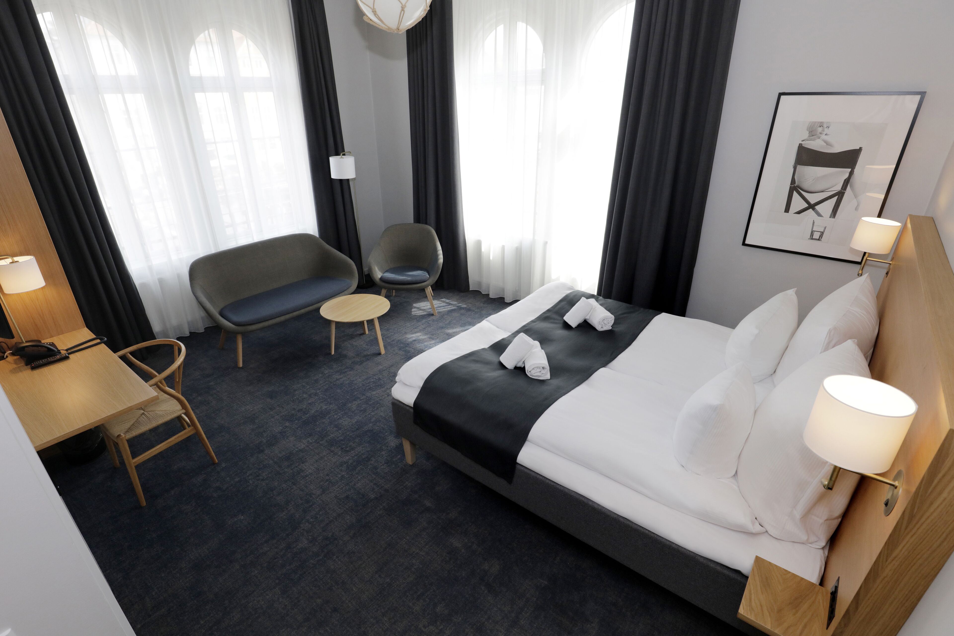 Quarto de hotel com uma cama, duas cadeiras, uma mesa pequena e uma escrivaninha.