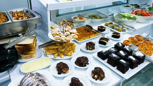 Buffet com diversos alimentos, incluindo pão, doces e sobremesas.