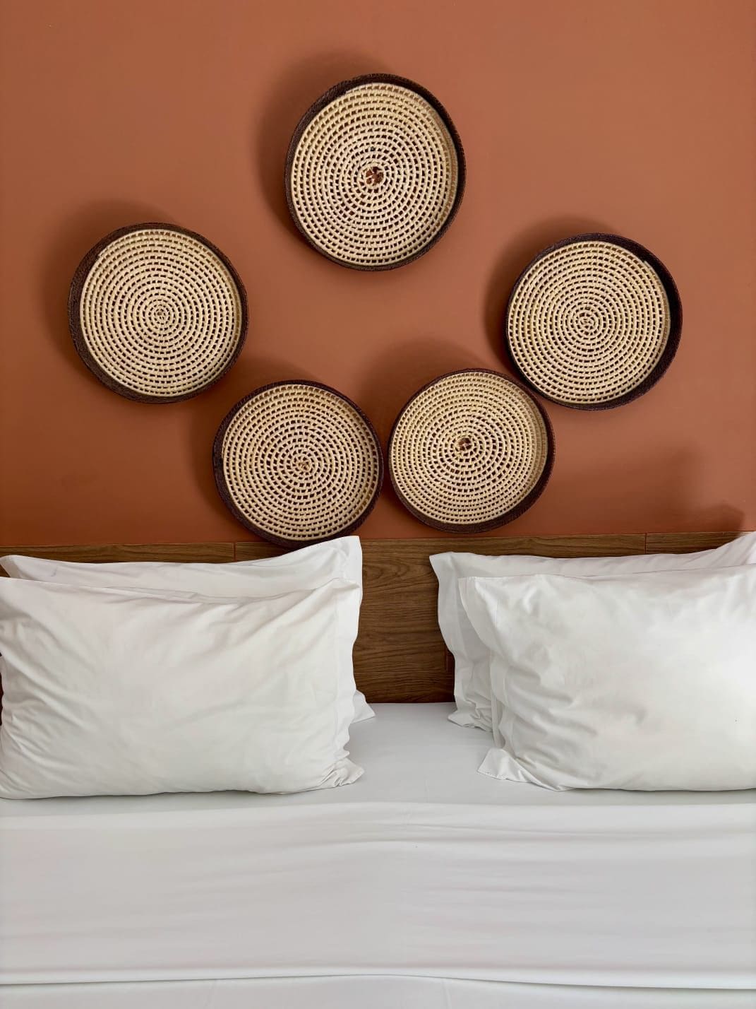 Cama com roupa de cama branca e duas almofadas, cabeceira de madeira e parede com cinco painéis de parede trançados.