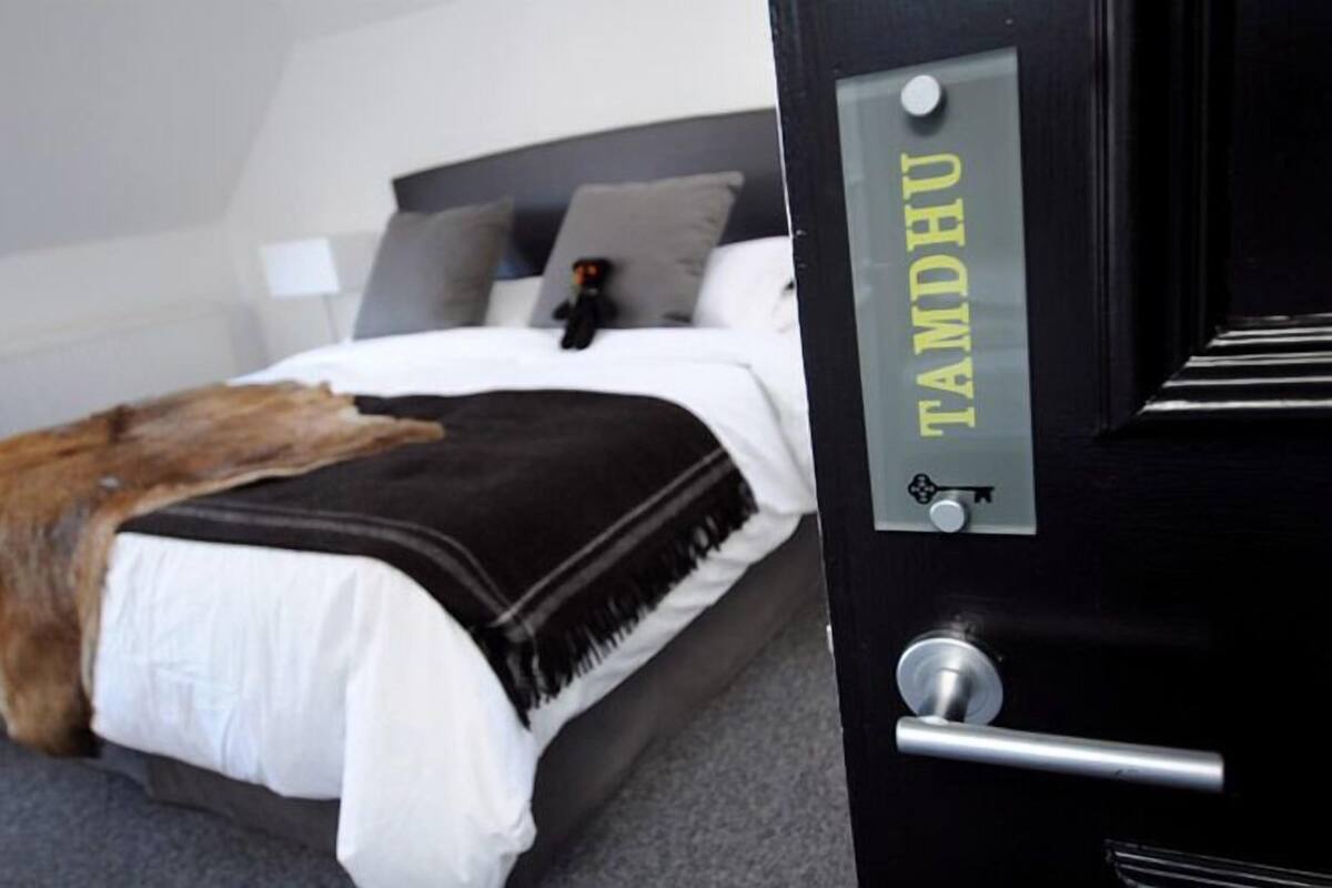 Quarto de hotel com uma cama, uma porta preta com placa de identificação e uma fechadura.