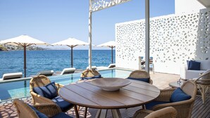 Piscina infinita com mobiliário de vime e guarda-sóis, com vista para o mar.