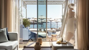 Quarto de hotel moderno com uma grande porta de vidro que dá para um terraço com guarda-sóis e vista para o mar.
