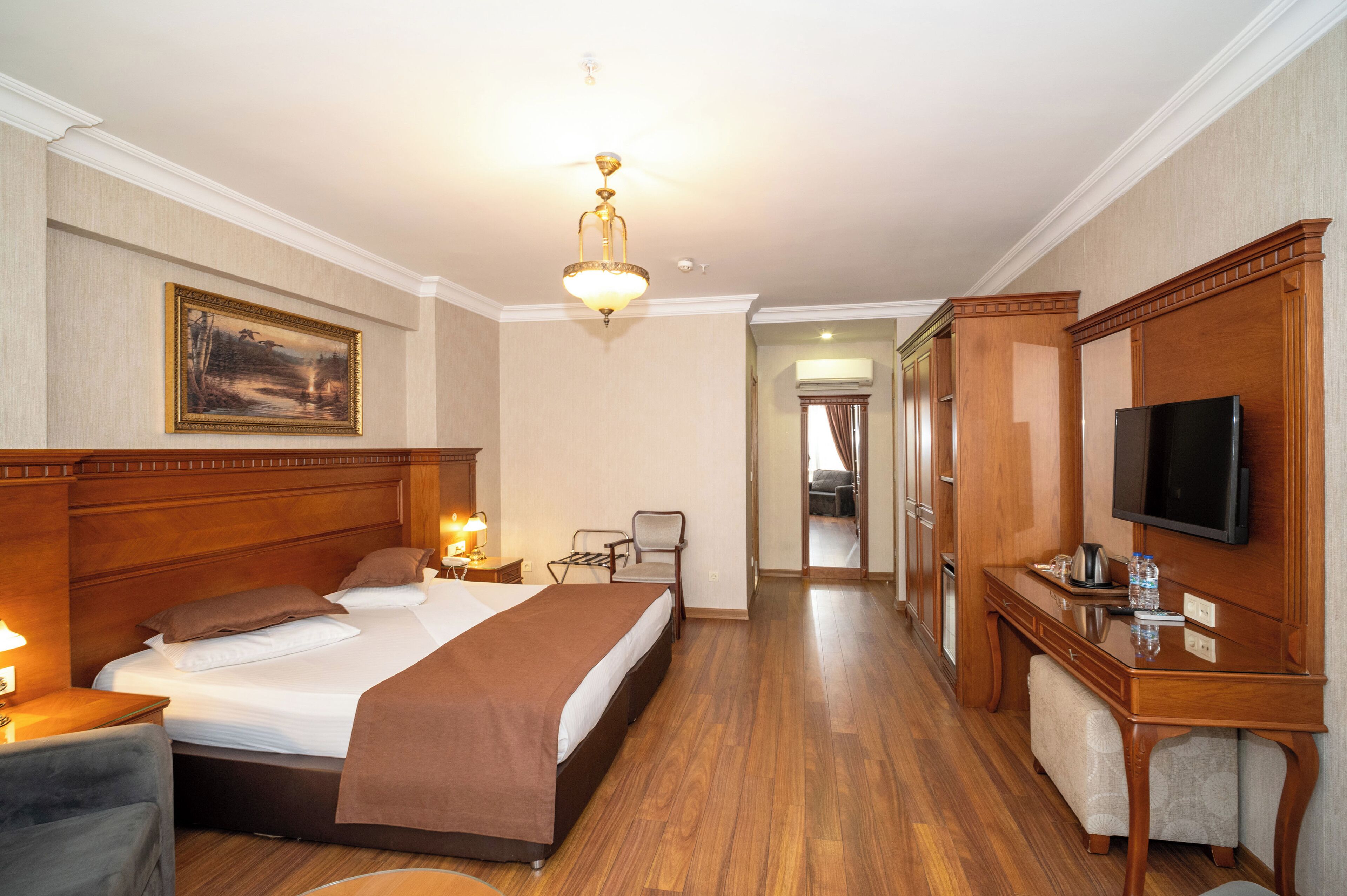Quarto de hotel com uma cama grande, mesas de cabeceira, uma escrivaninha com televisão de tela plana, uma cadeira e um quadro na parede.