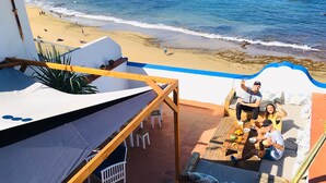 Um terraço com vista para a praia, mobiliário de exterior e uma mesa com comida.