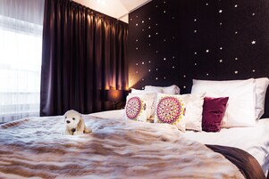 Quarto de hotel com cama, tapete fofinho, mesa de cabeceira e parede decorada com estrelas.