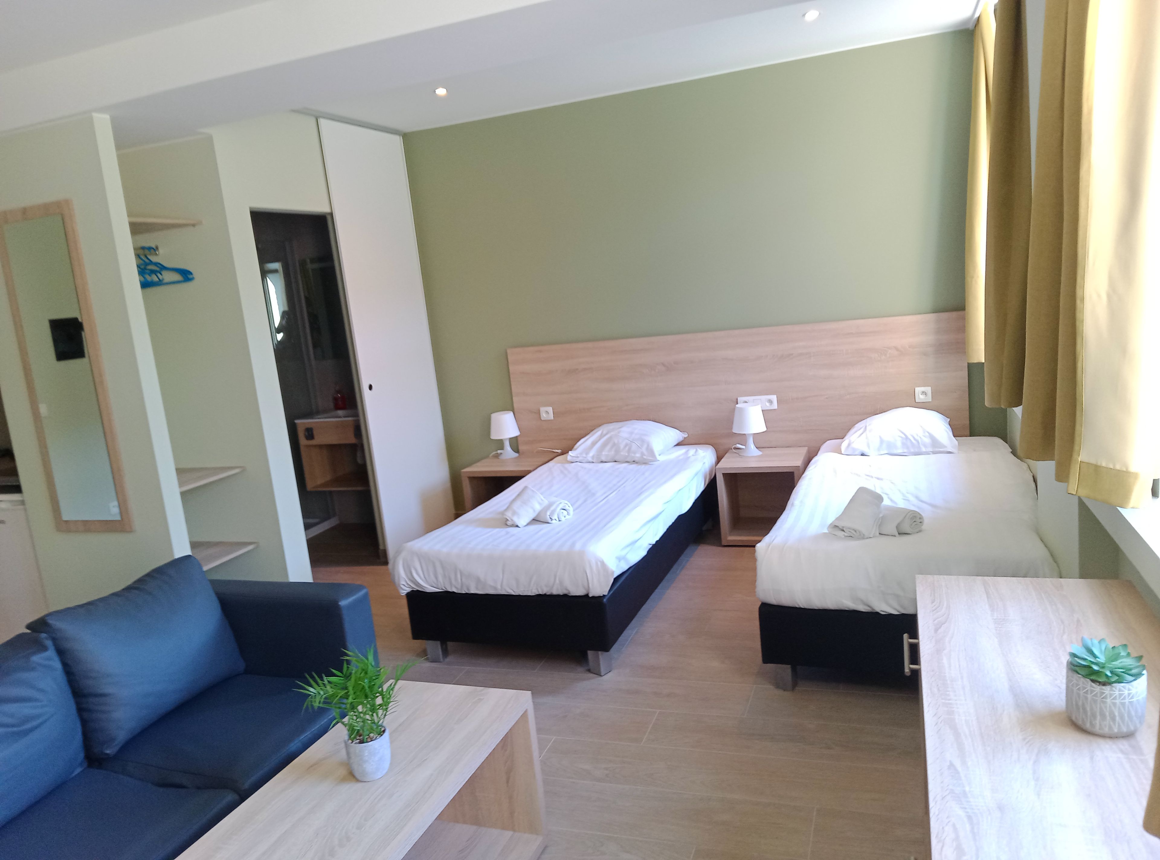 Quarto de hotel com duas camas, um sofá, uma mesa pequena e um vaso de planta.