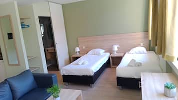 Quarto de hotel com duas camas, um sofá, uma mesa pequena e um vaso de planta.