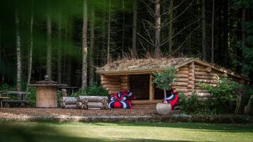Uma cabana de toras com telhado de palha, rodeada por uma floresta.