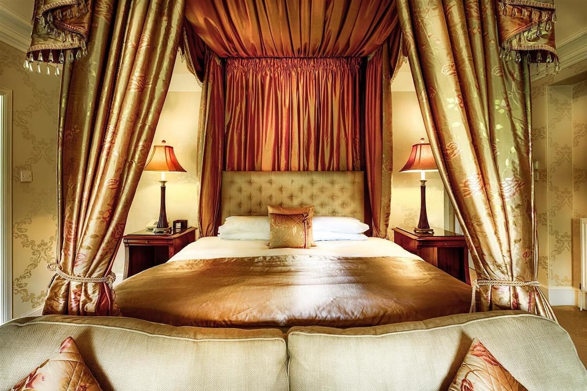 Um quarto luxuoso com cama de dossel, cortinas elaboradas e luminárias combinando.