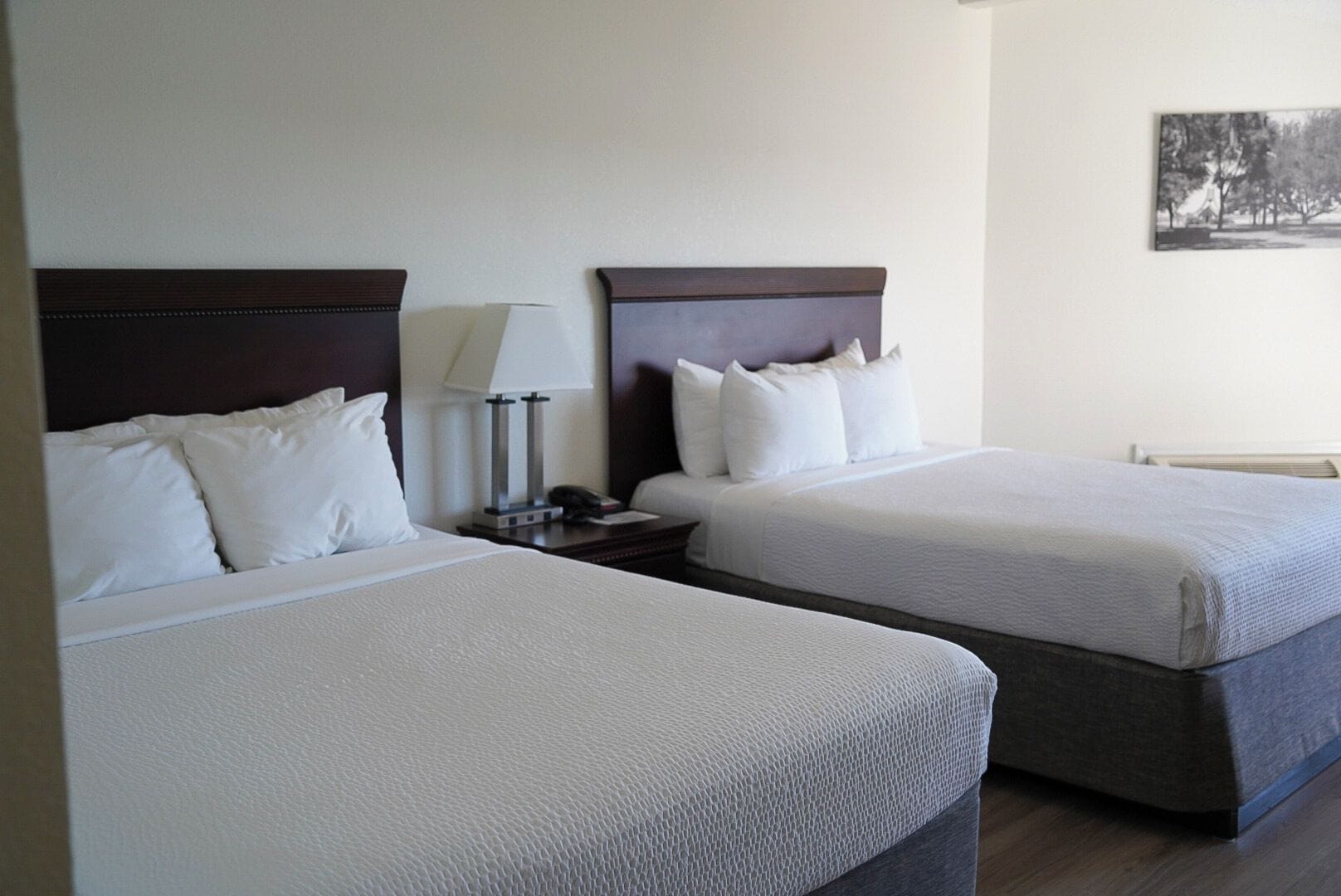 Quarto de hotel com duas camas, cada uma com roupa de cama branca e cabeceiras escuras. Há uma mesa de cabeceira com abajur e telefone.