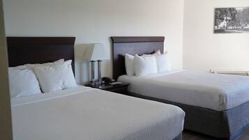 Quarto de hotel com duas camas, cada uma com roupa de cama branca e cabeceiras escuras. Há uma mesa de cabeceira com abajur e telefone.