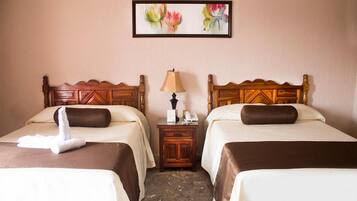 Quarto de hotel com duas camas, uma mesa de cabeceira com abajur e uma pintura floral emoldurada na parede.