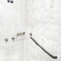 Casa de banho com azulejos de mármore branco, um corrimão e painel de comando do chuveiro.