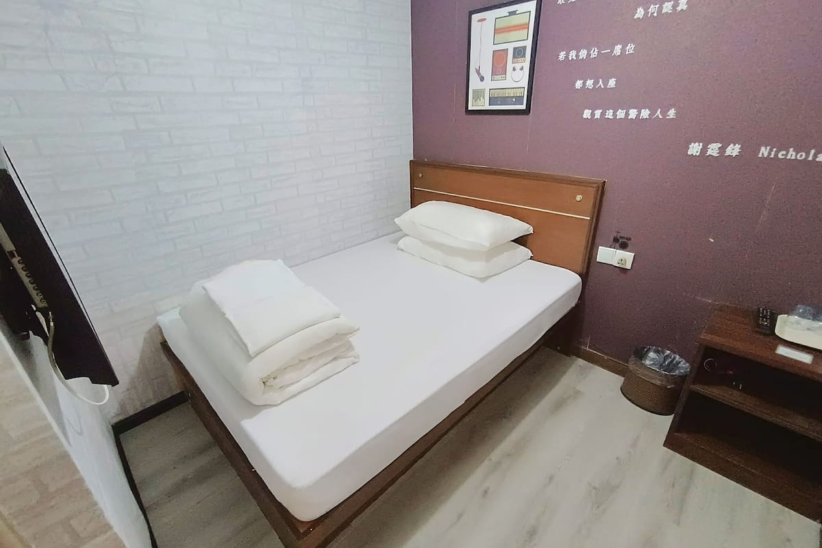 Cama bem arrumada com lençóis brancos num quarto com parede de tijolos e uma parede de destaque roxa.
