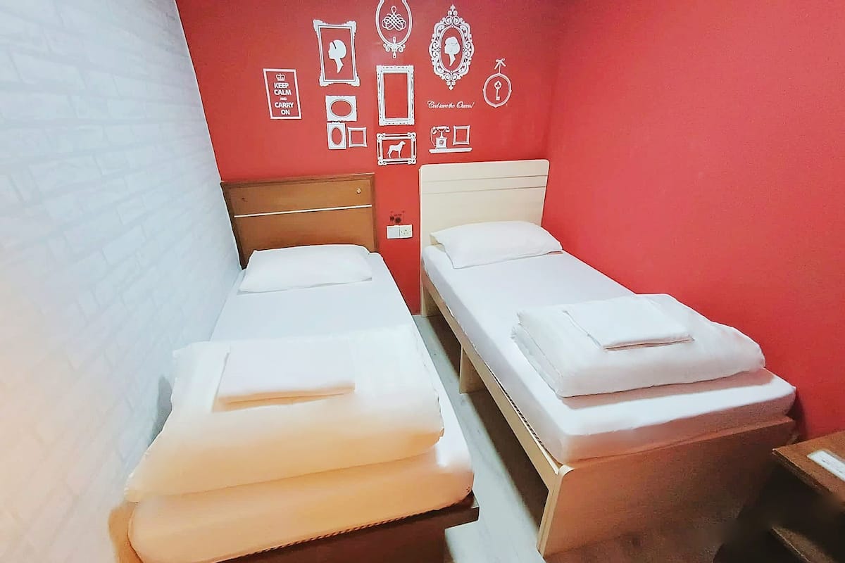 Quarto com duas camas de solteiro, cabeceira de madeira, parede vermelha com arte decorativa e parede de tijolos brancos.