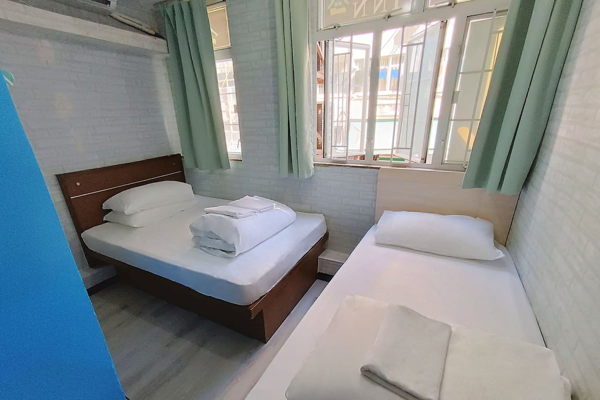 Quarto de hotel com duas camas, uma janela com cortinas e vista para o exterior.