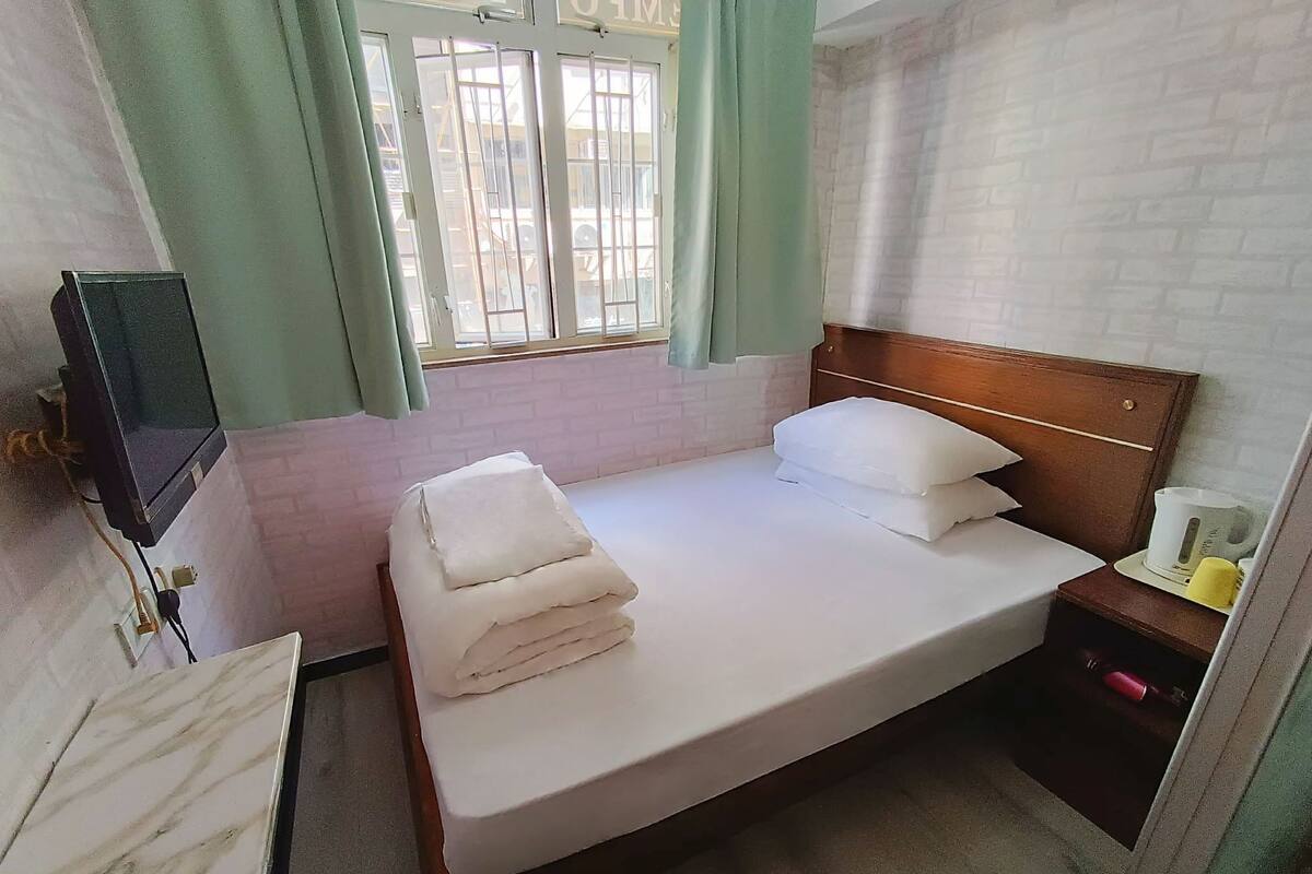 Quarto de hotel com cama, televisão, mesa de cabeceira e janela com cortinas.