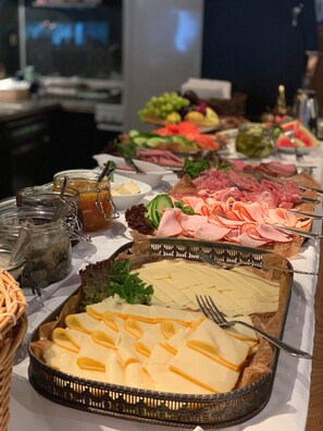 Mesa de buffet com diversos alimentos, incluindo carnes, queijos e frutas.