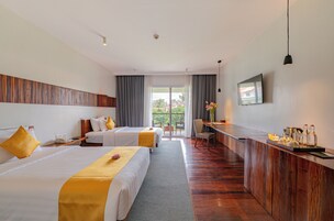 Quarto de hotel com duas camas, uma mesa, uma TV e vista para o verde lá fora.