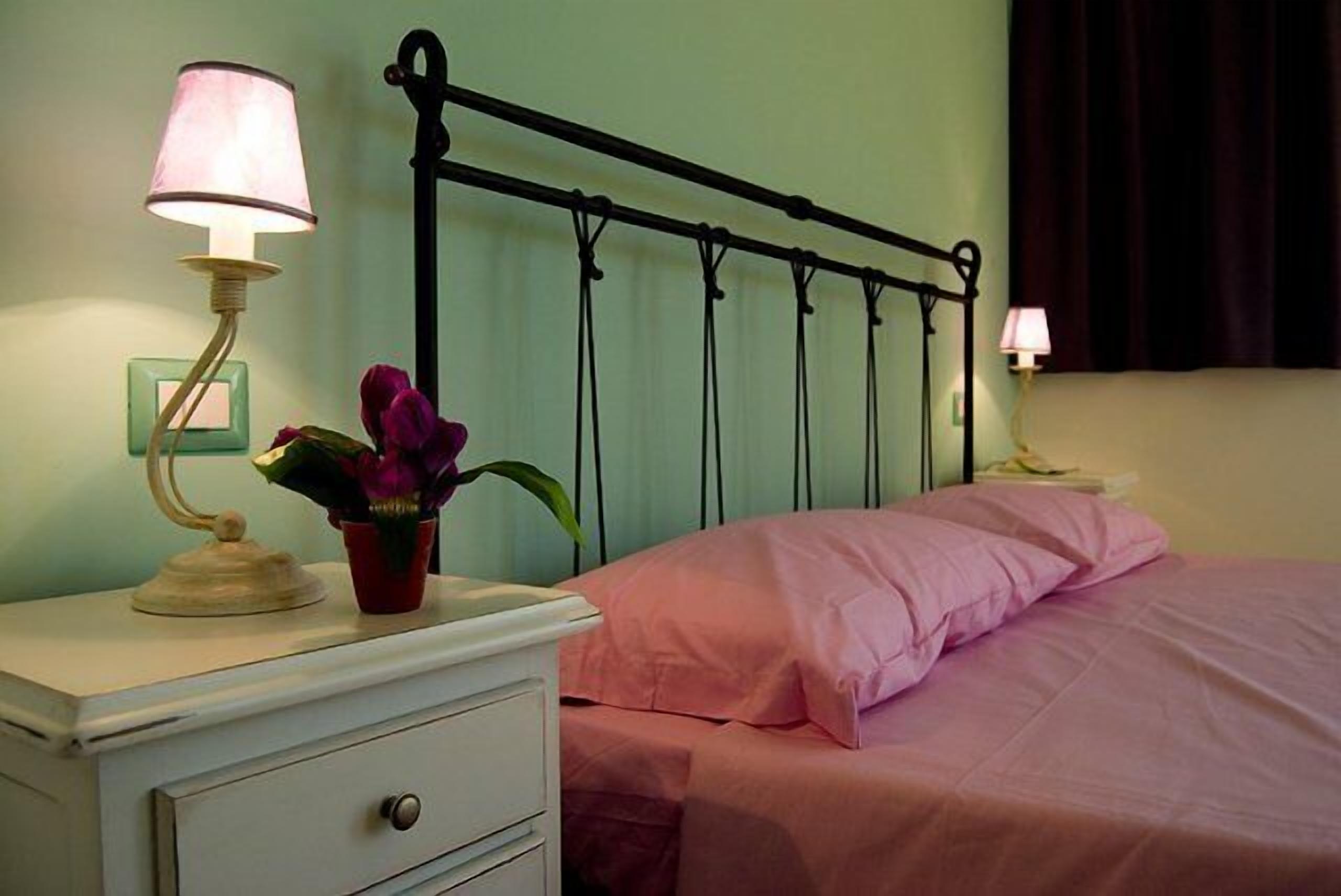 Um quarto com uma cama, uma mesinha de cabeceira, um abajur e um vaso de plantas.