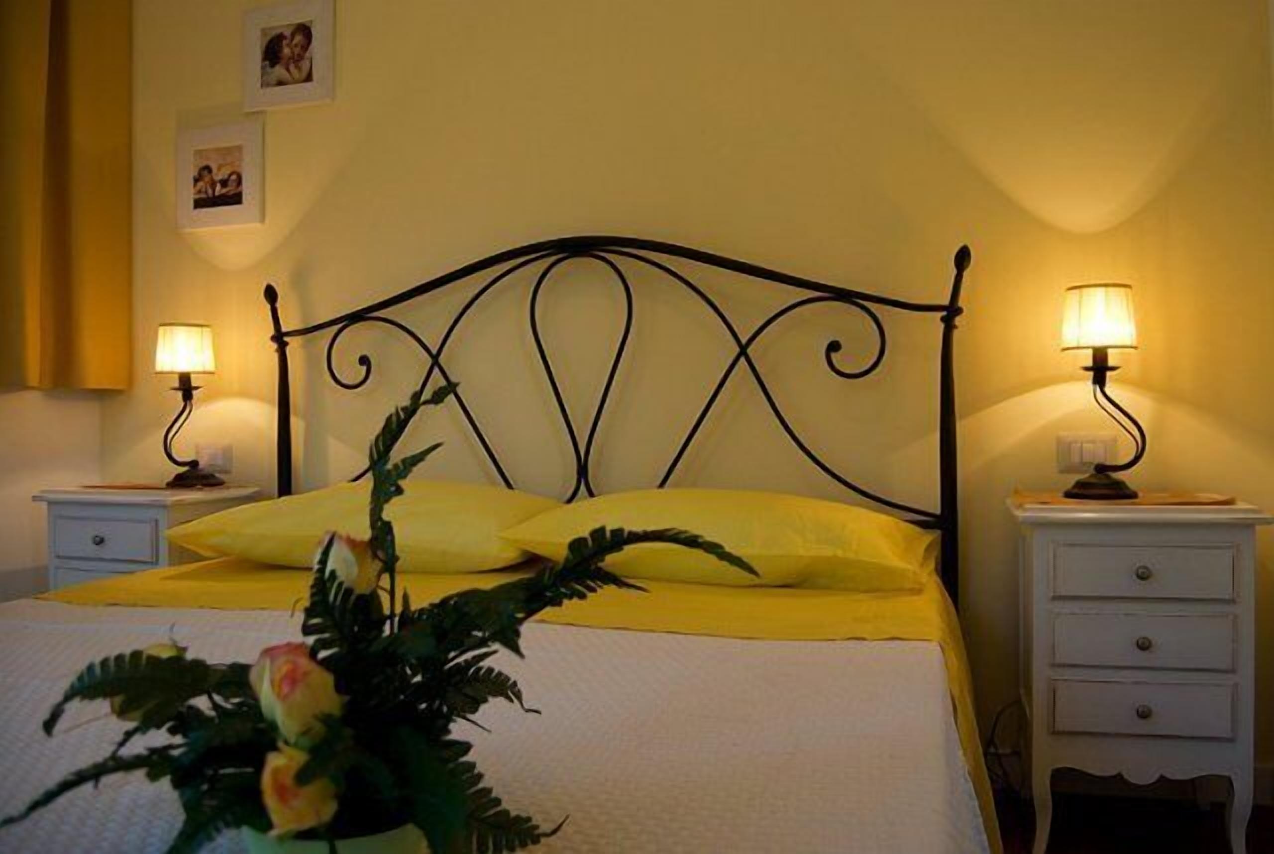 Cama bem arrumada com almofadas amarelas, cabeceira de metal preto e duas luminárias de cabeceira.