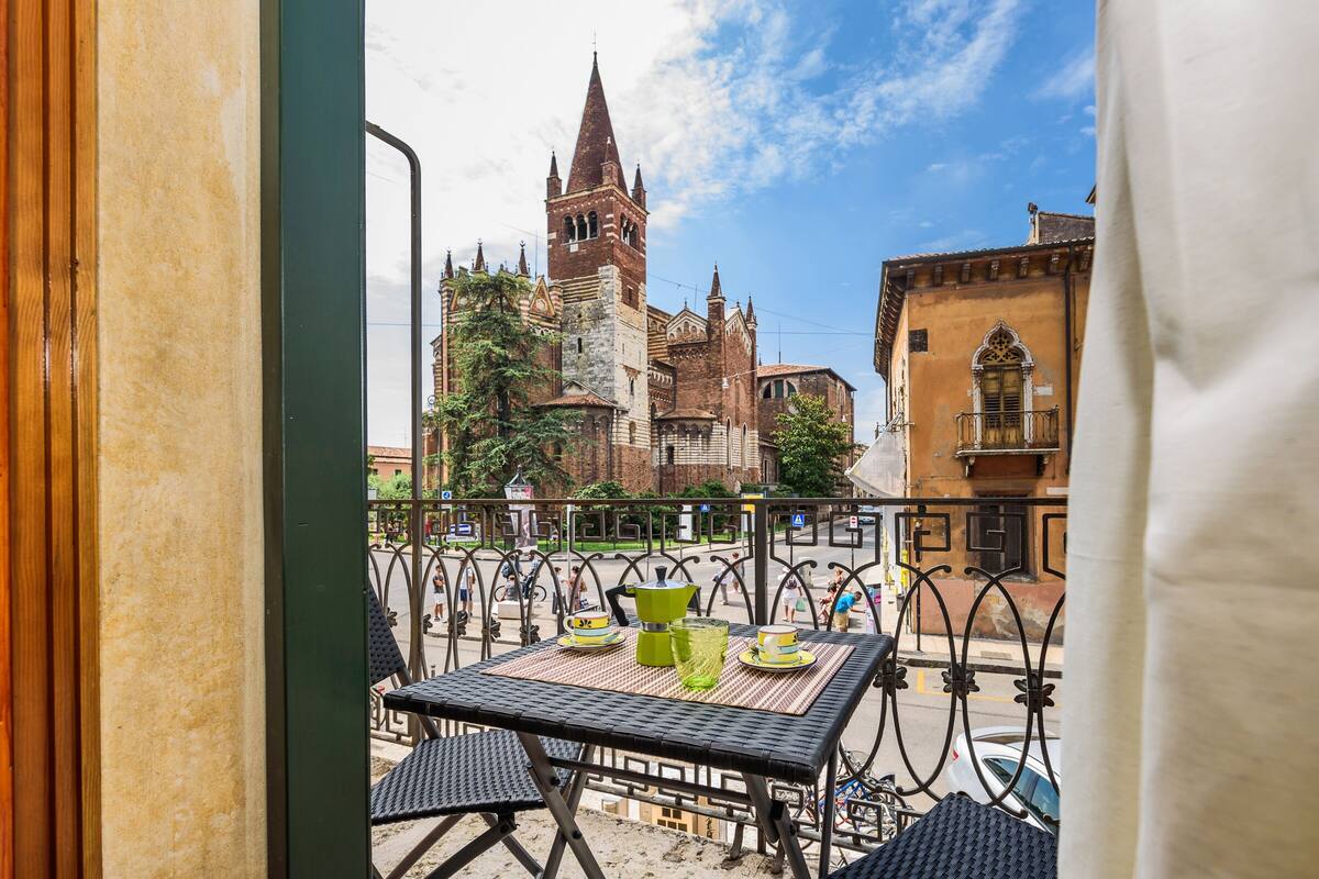 Varanda com mesa posta para dois, com vista para uma igreja histórica e uma alta torre do sino.