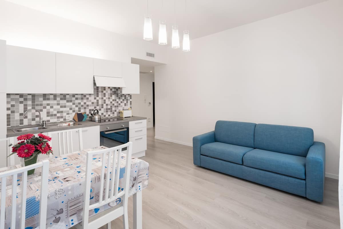Uma cozinha moderna com armários brancos, painel de azulejos e um sofá azul na sala de estar.
