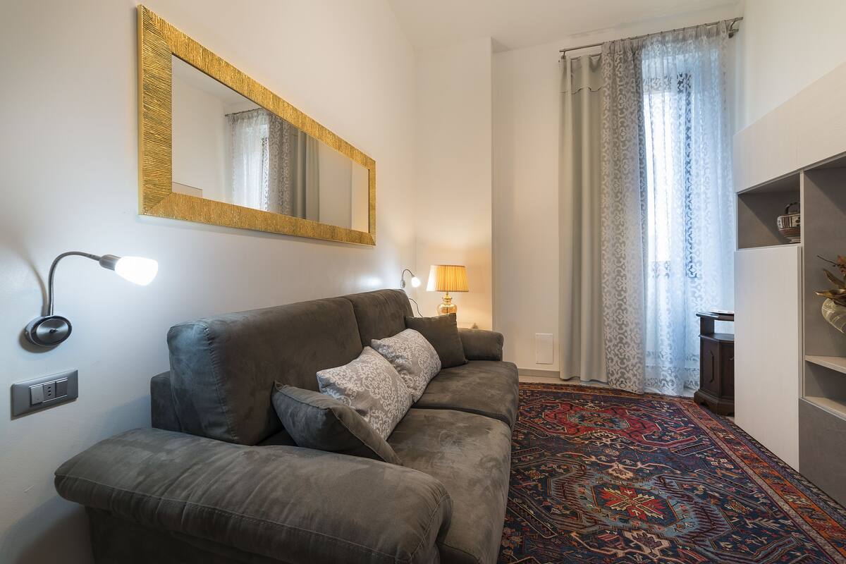 Sala de estar com um sofá, um espelho grande, um abajur e um tapete estampado.