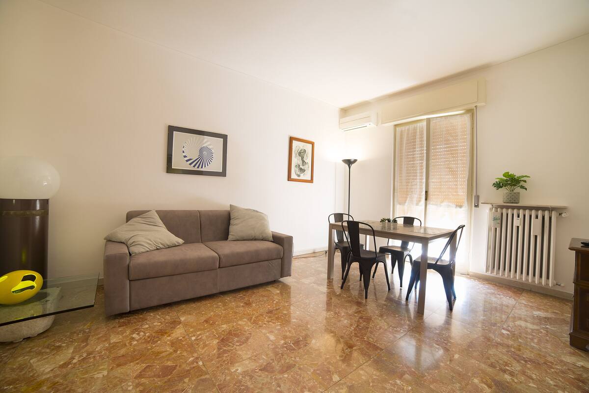 Uma sala de estar com sofá, mesa de jantar, cadeiras e radiador.