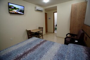 Um quarto pequeno com uma cama, uma escrivaninha, uma cadeira e uma televisão na parede.