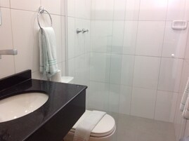 Casa de banho com bancada preta, lavatório branco, sanita e cabine de duche em vidro.