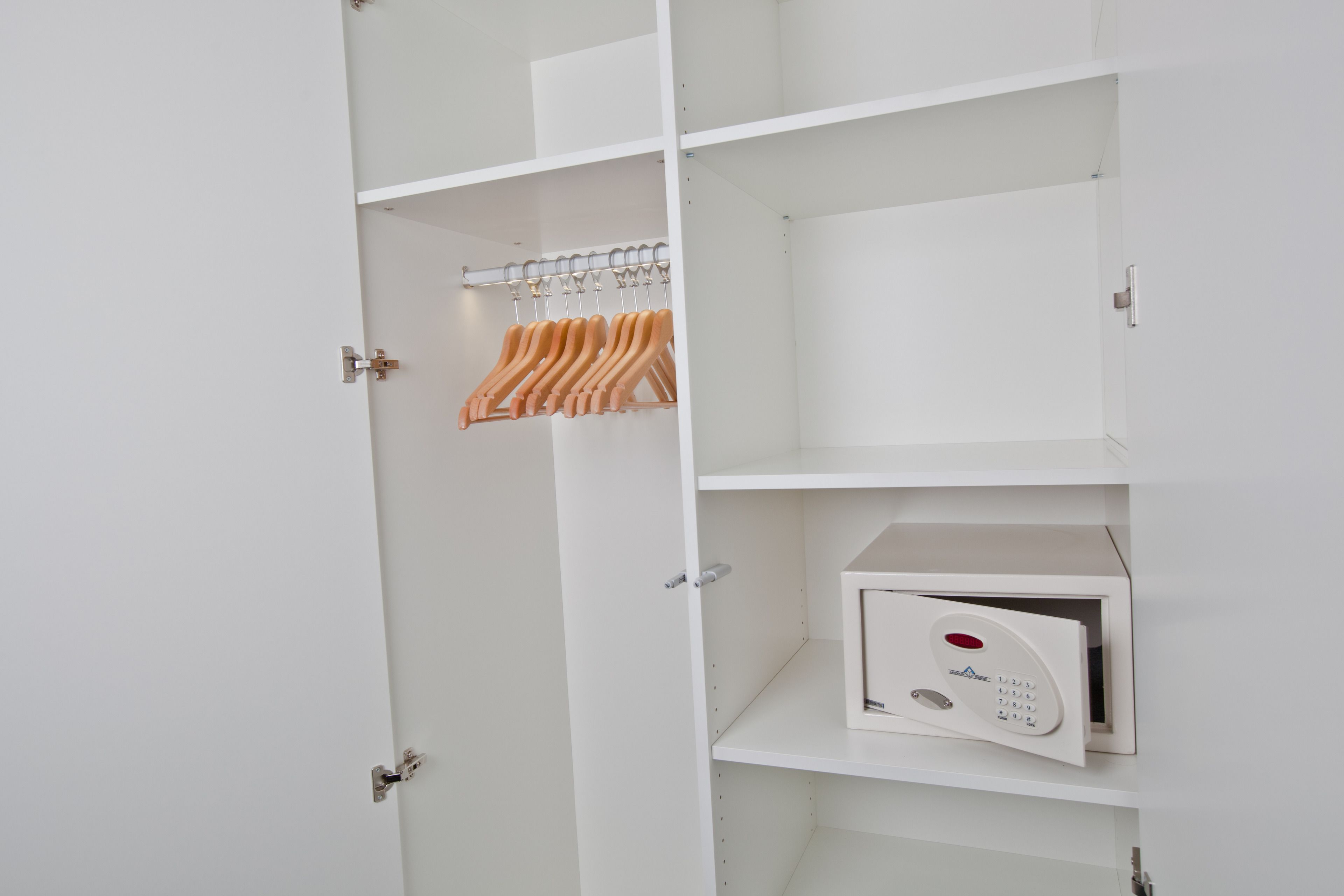 Um guarda-roupa branco com várias prateleiras, cabideiro e um cofre embutido.