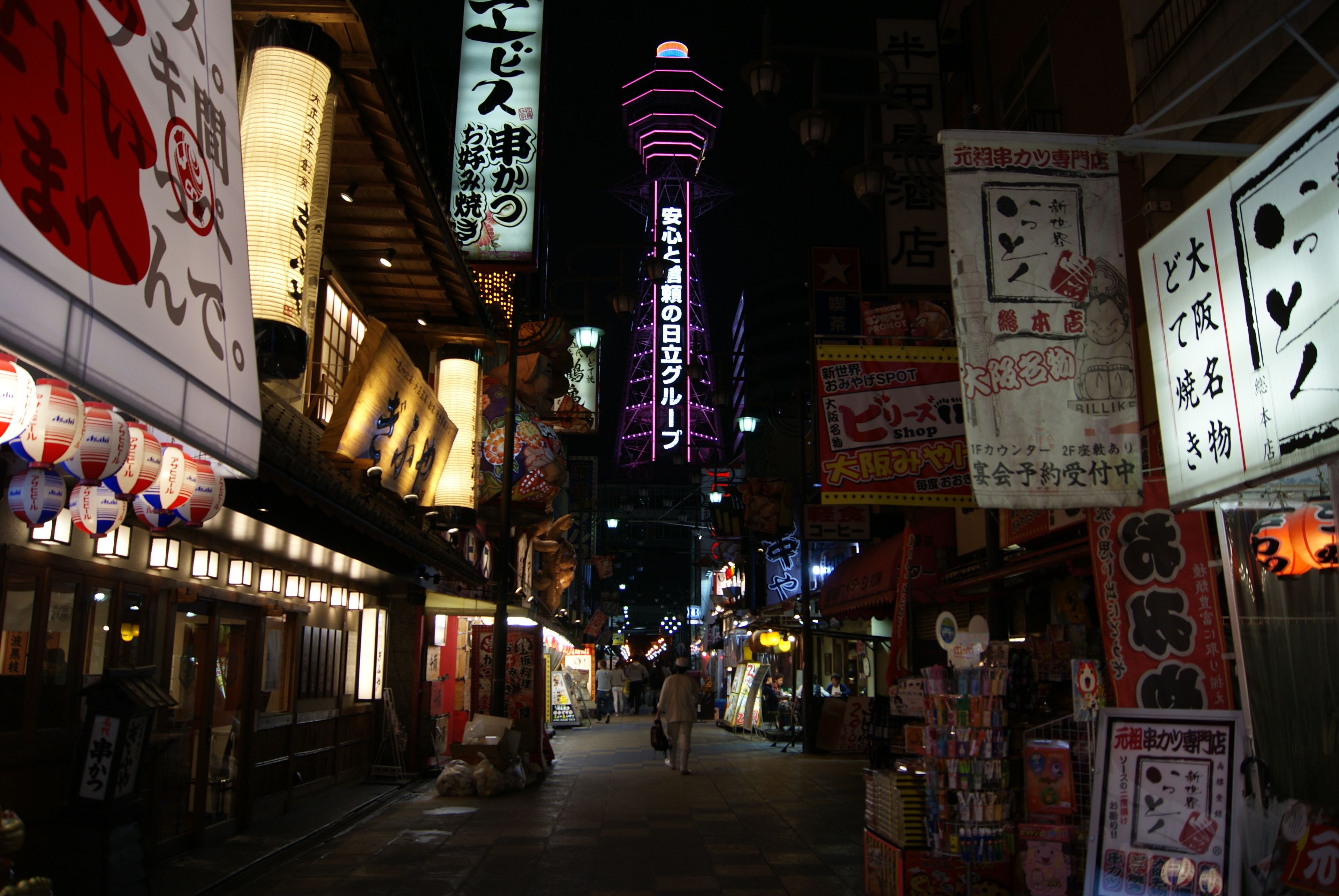 Uma rua estreita com lojas tradicionais japonesas e letreiros iluminados.