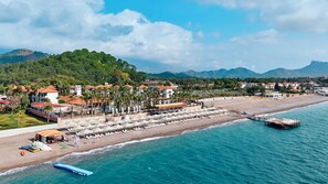 Um resort à beira-mar com uma fileira de espreguiçadeiras, uma torre de salva-vidas e um píer que se estende para o mar.