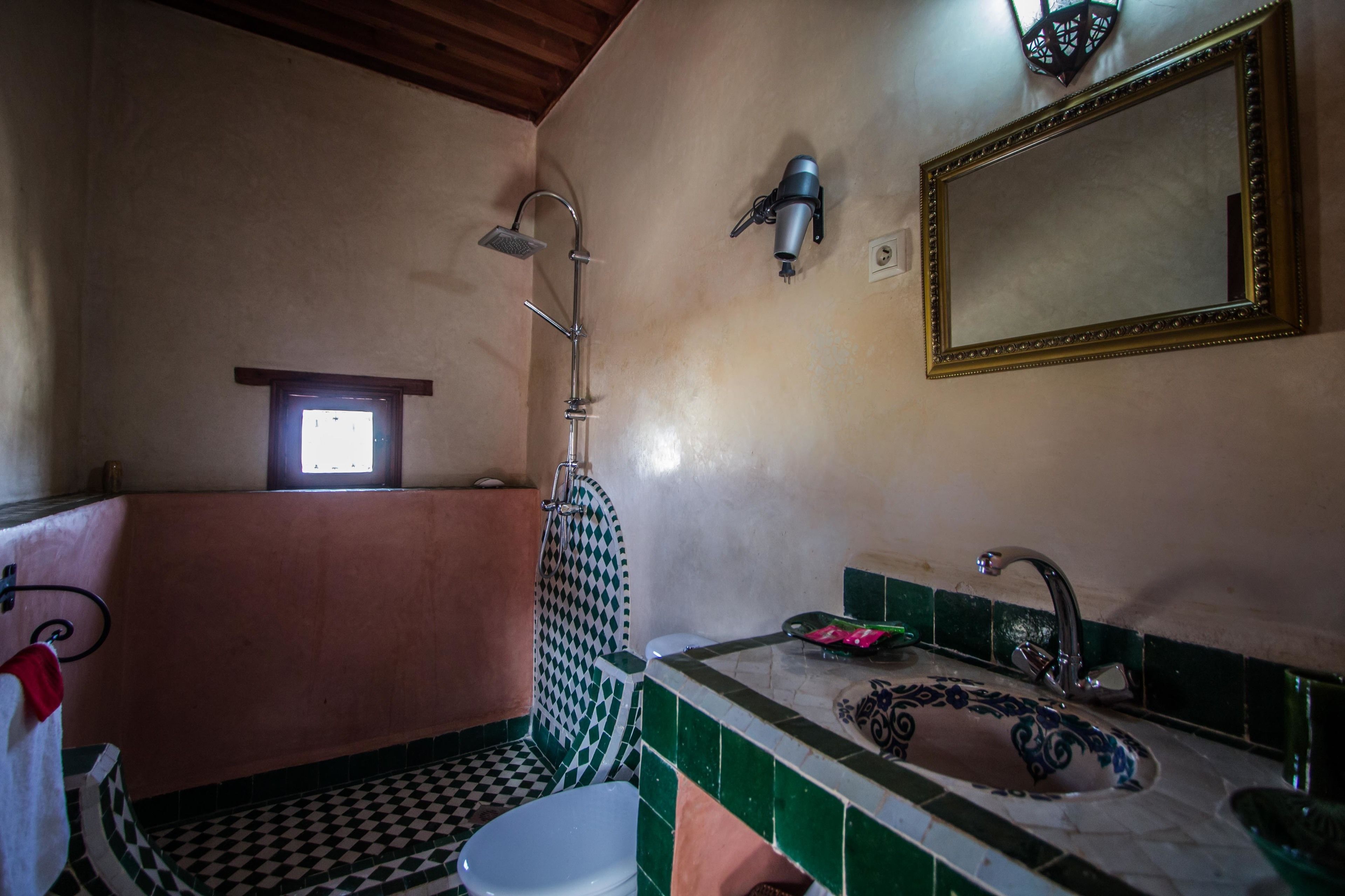 Casa de banho com chuveiro, sanita, lavatório e espelho.