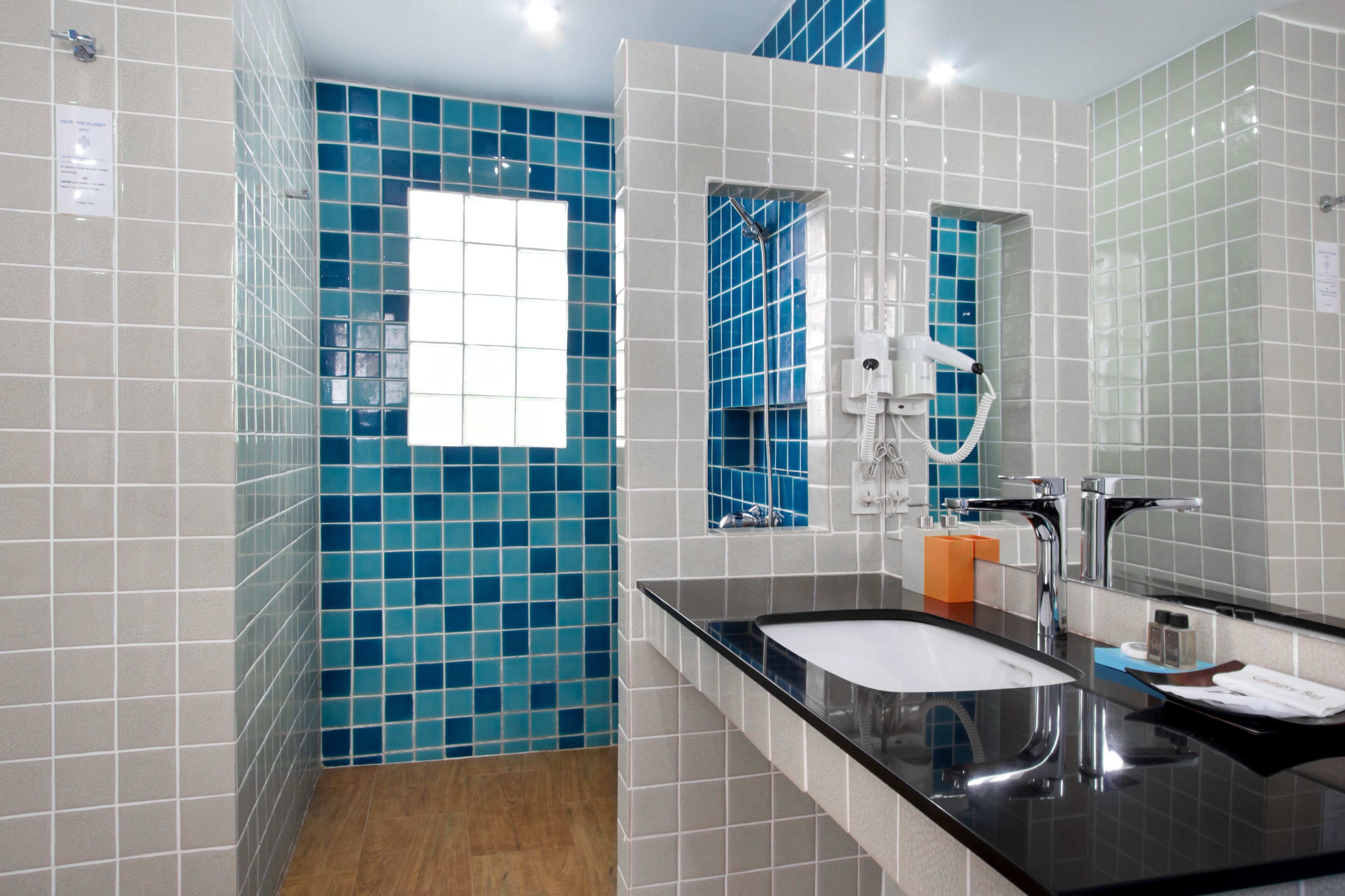 Casa de banho moderna com lavatório preto, azulejos brancos e azuis, e uma janela.