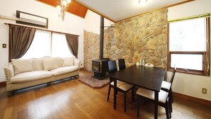 Uma sala de estar com sofá, mesa de jantar, cadeiras, parede de pedra e lareira.