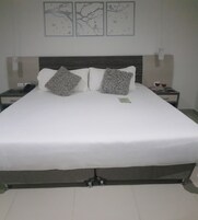 Cama bem arrumada com cabeceira escura, dois travesseiros e uma pequena placa verde na cama.