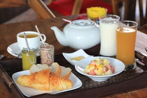Bandeja de café da manhã com croissants, salada de frutas, leite, chá e uma chaleira.