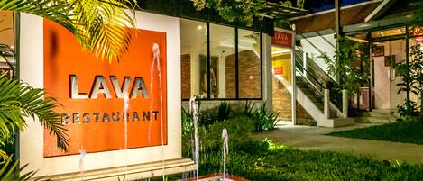 Um restaurante chamado Lava, com uma placa, um espelho d'água e uma escadaria que leva à entrada.