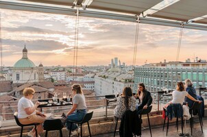 Terraço no telhado com vista para a cidade, mesas, cadeiras e guarda-corpo.