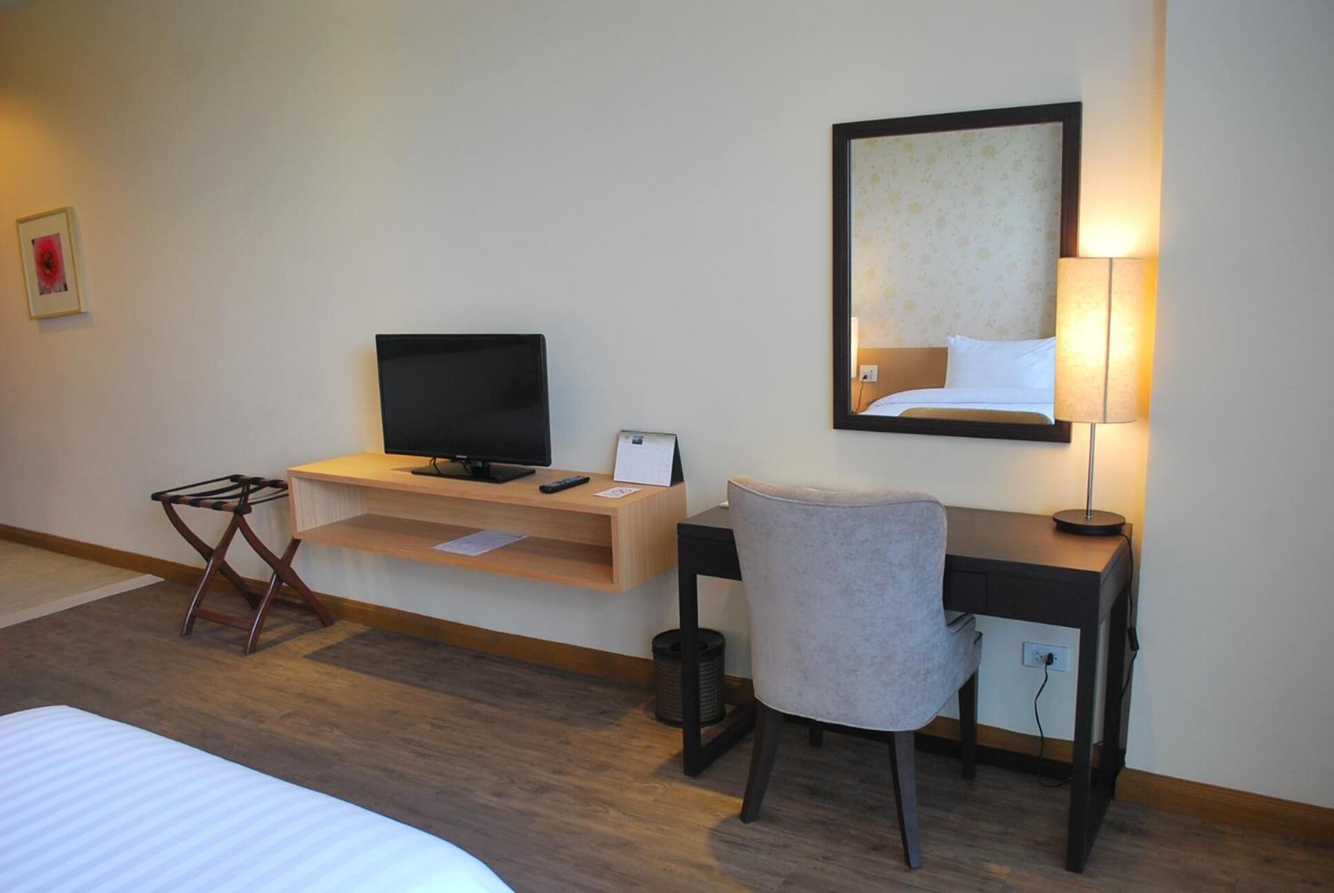 Quarto de hotel com cama, escrivaninha com computador, televisão, cadeira e abajur.