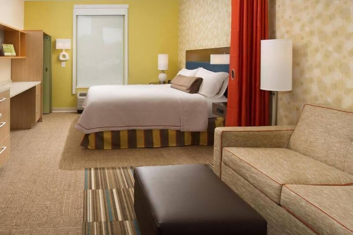 Quarto de hotel com cama, sofá, escrivaninha e janela.