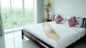 Uma cama bem arrumada com lençóis brancos, um vaso decorativo com flores e vista para um verdejante jardim através de grandes janelas.