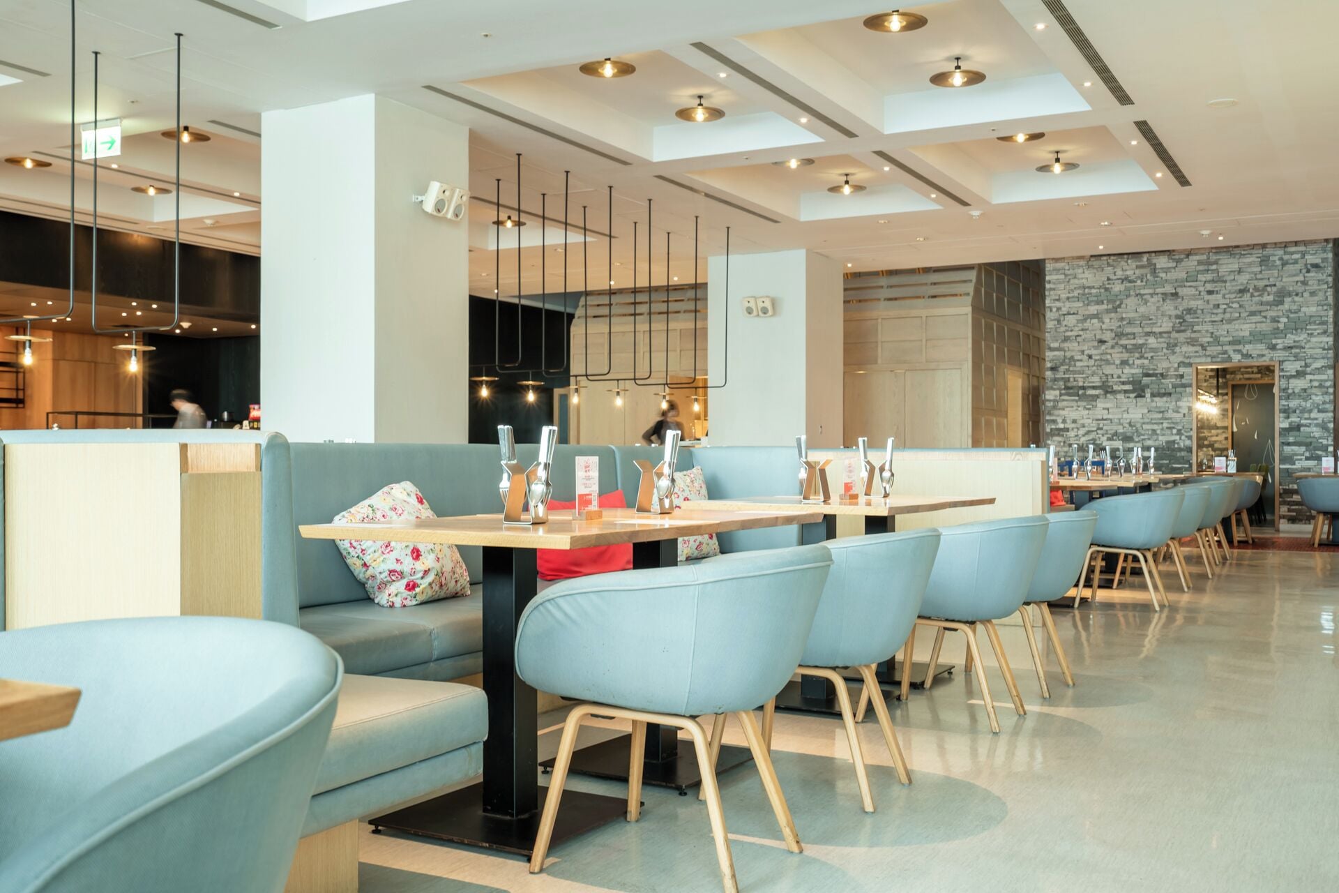 Um restaurante moderno com um balcão extenso, assentos estofados em azul e uma parede de destaque em pedra.