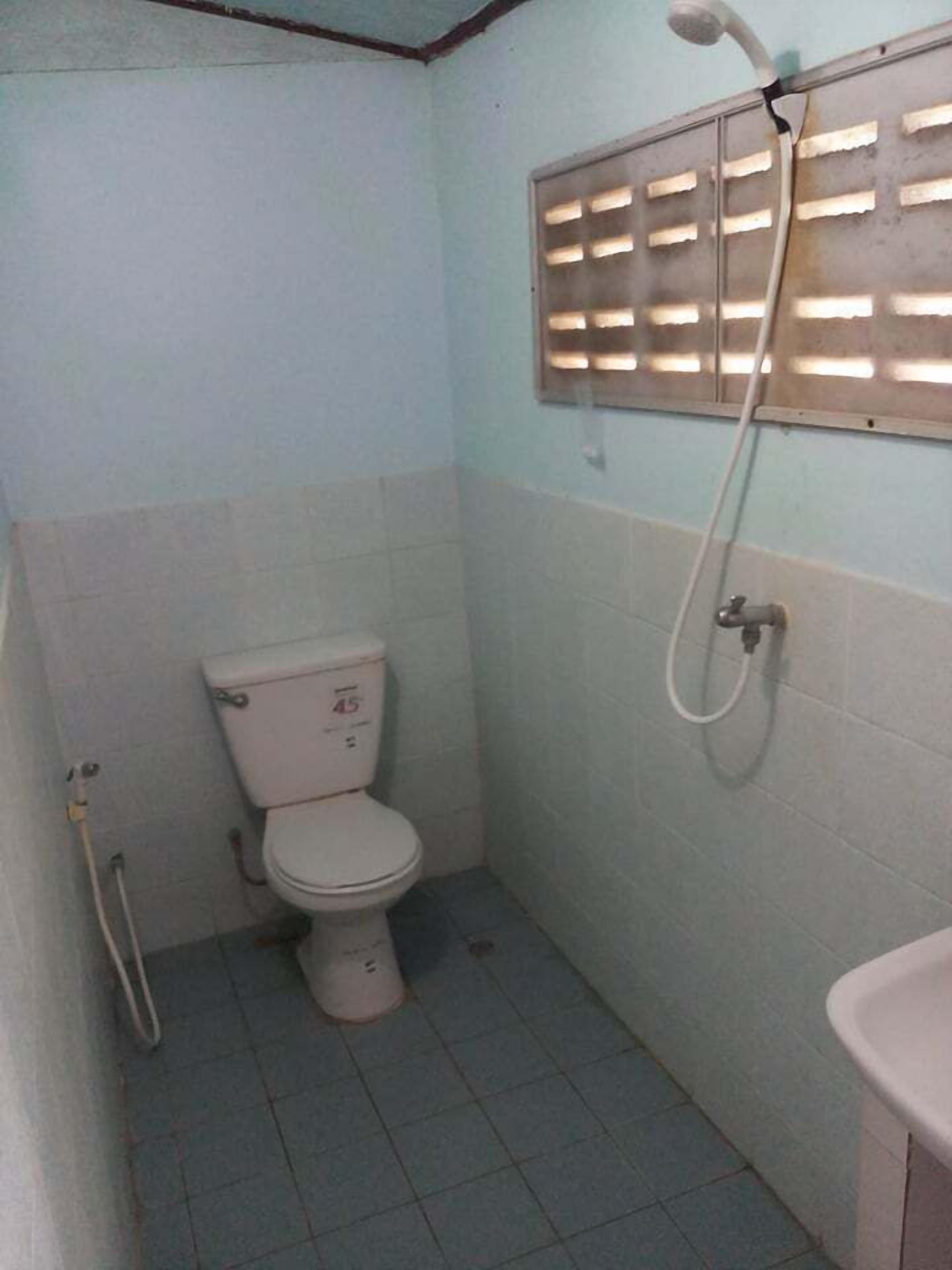Uma casa de banho pequena e simples, com sanita, chuveiro e lavatório.