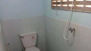 Uma casa de banho pequena e simples, com sanita, chuveiro e lavatório.